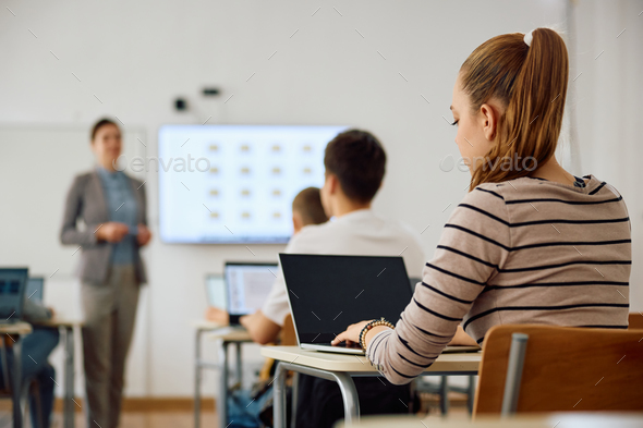 Rear view of female high school student learning computer programing during IT class in ...